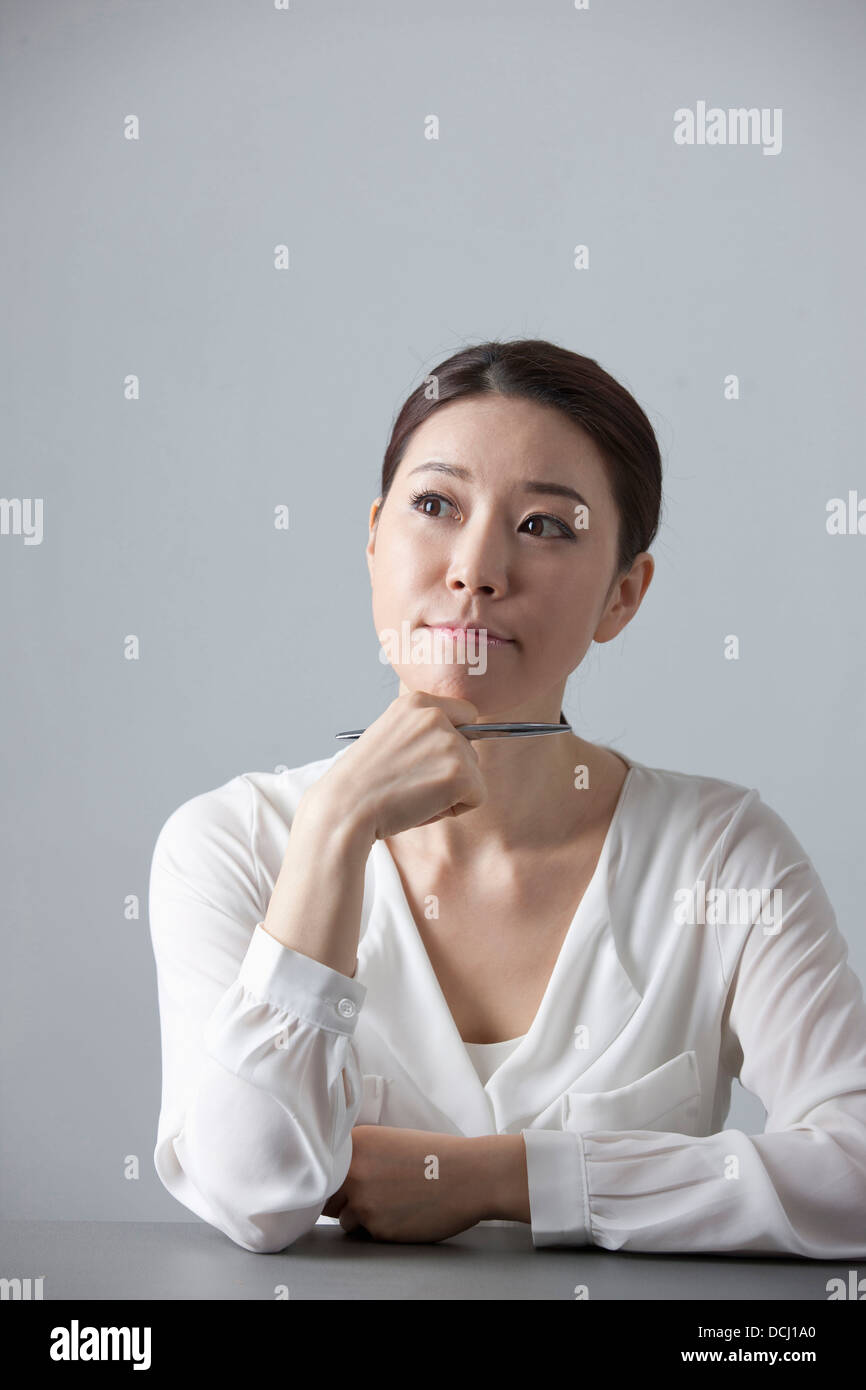 a woman thinking while sitting at a desk Stock Photo - Alamy