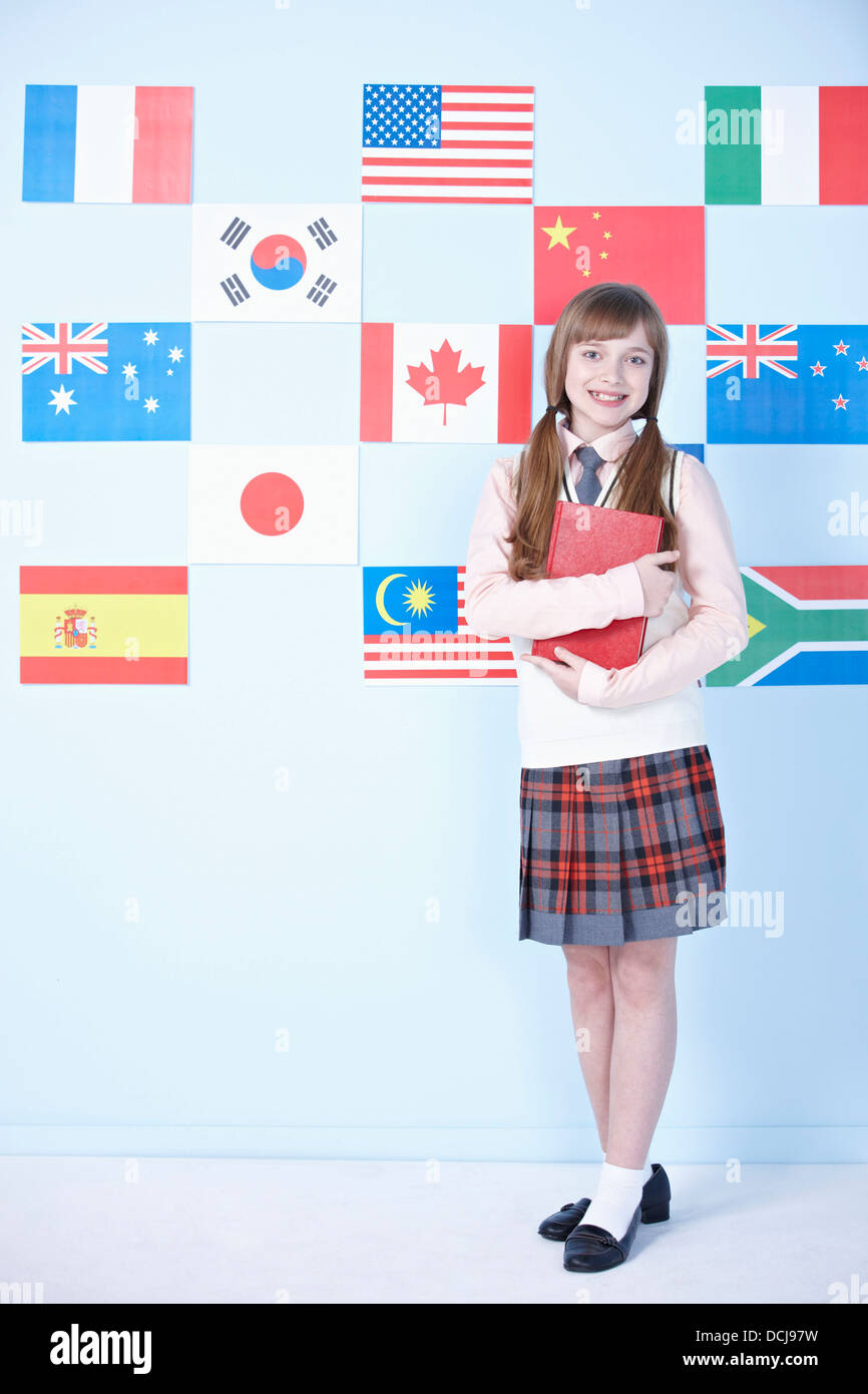 a student in uniform posing in front of international flags with a book ...