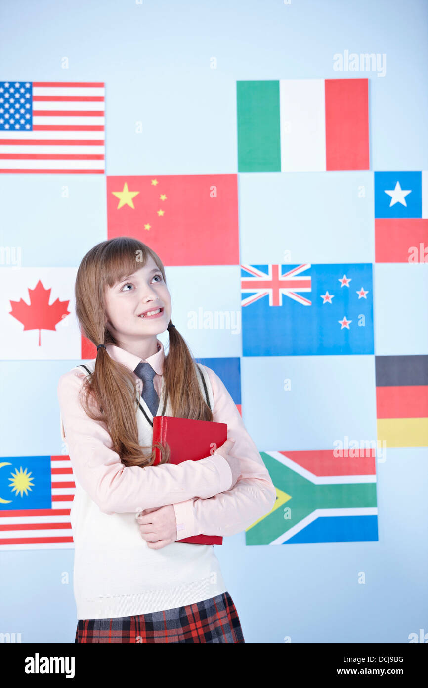 a student in uniform posing in front of international flags with a book ...