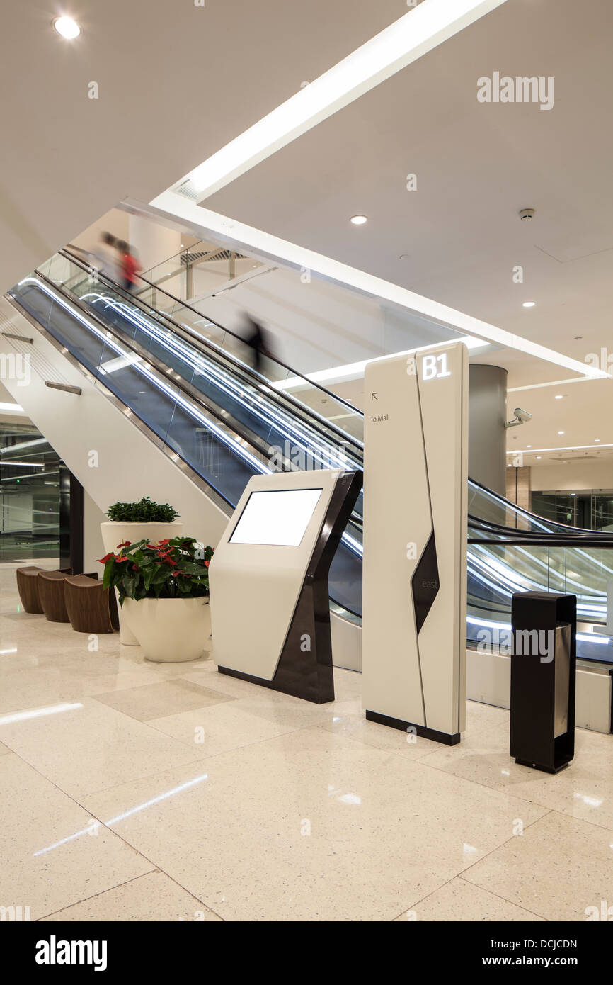 people on the escalator at the mall.plants,screens and stools around ...