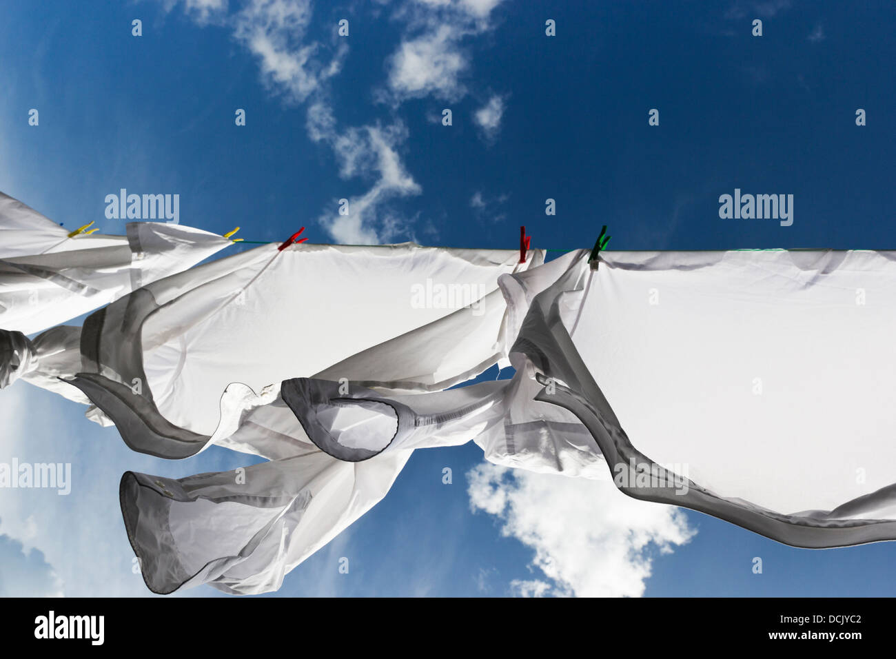 White shirts hanging on washing line against a blue sky with fluffy ...