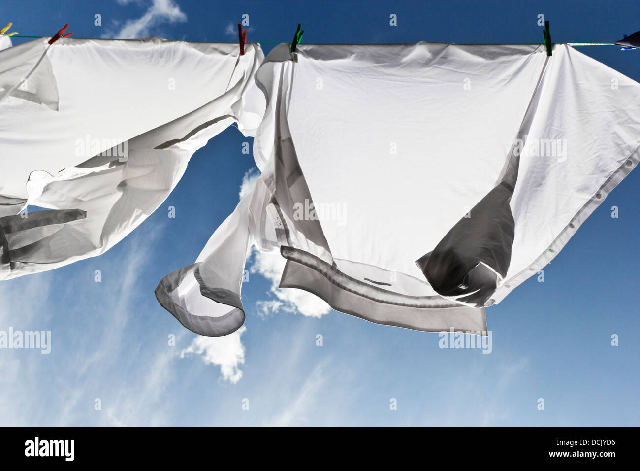 White shirts hanging on washing line against a blue sky with fluffy and ...