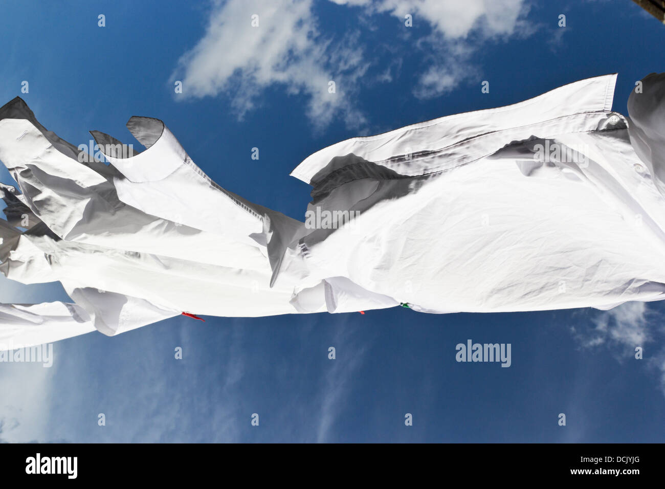 White shirts hanging on washing line against a blue sky with fluffy and ...