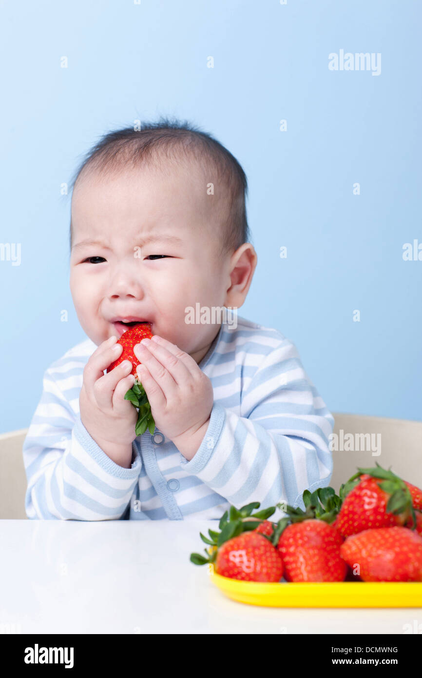 a baby crying while having a strawberry Stock Photo - Alamy