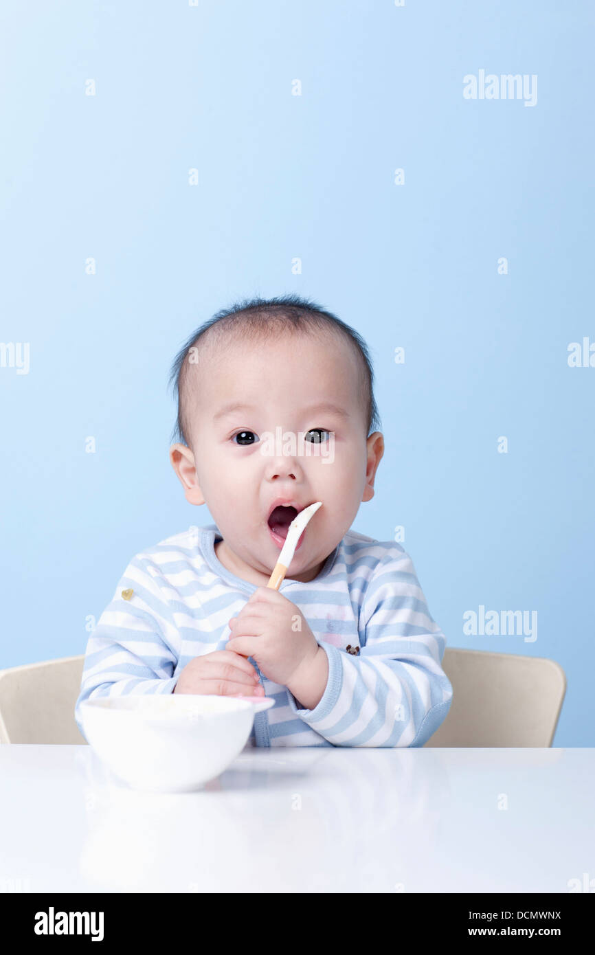 a baby with a bowl and a spoon on table Stock Photo - Alamy