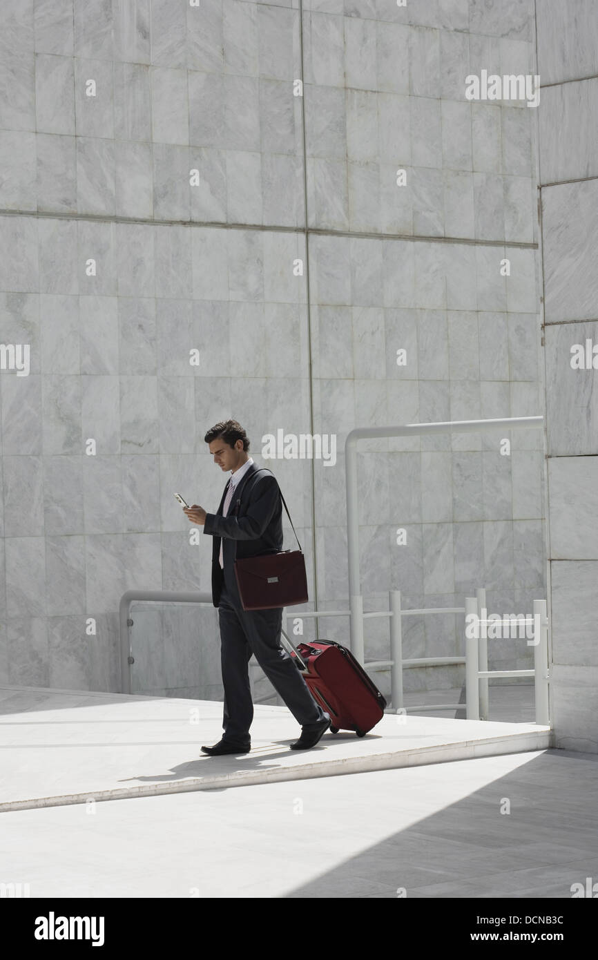 Businessman walking with a suitcase and cell phone Stock Photo - Alamy