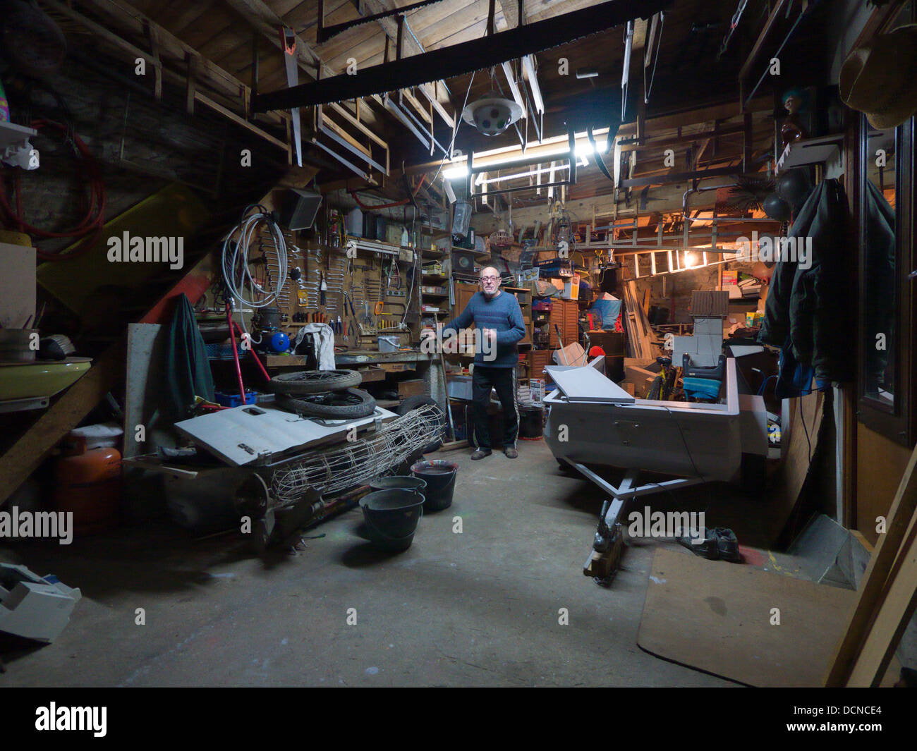 A man in his garage workshop surrounded by tools and implements in a ...