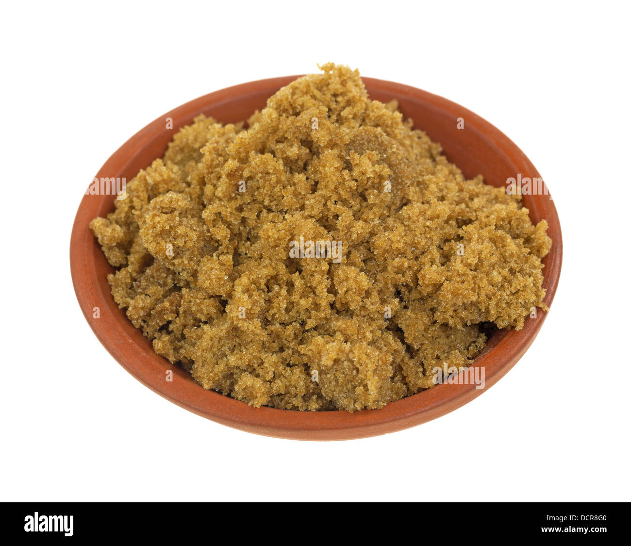 A small red clay bowl filled with clumpy dark brown sugar on a white ...