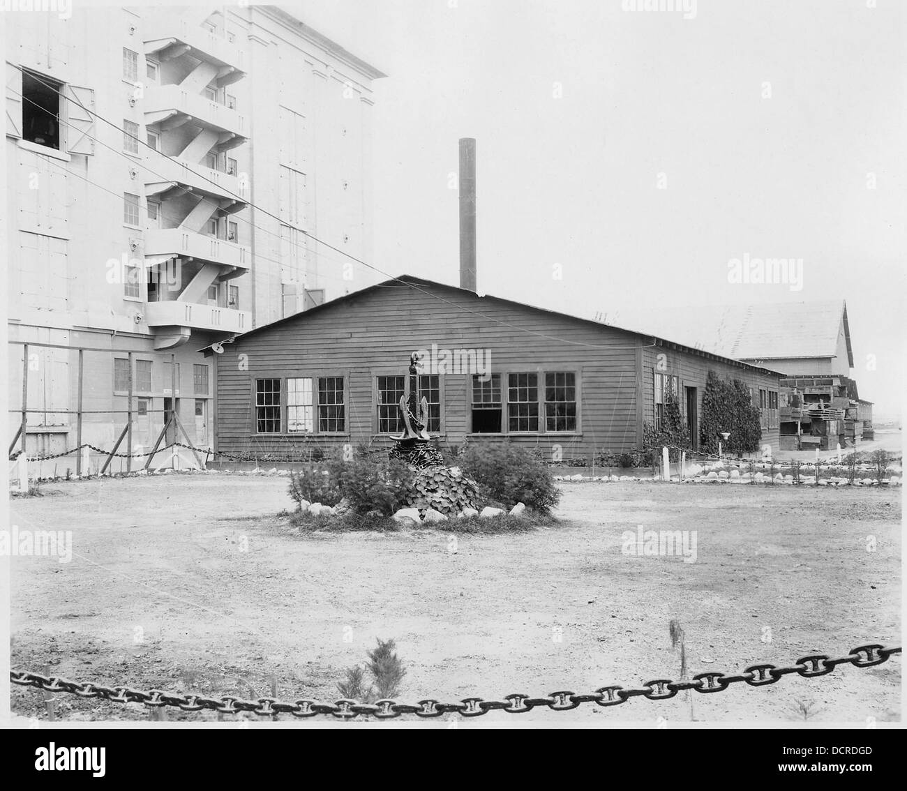 The image shows a single-story wood building next to a modern barracks ...