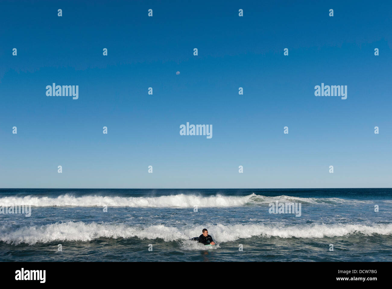 Surfer lying on board, surfing in from the ocean at Kiama Surf Beach ...