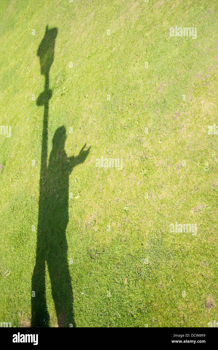 Shadow of a man on a lawn leaning against a lamp post with his hand out ...