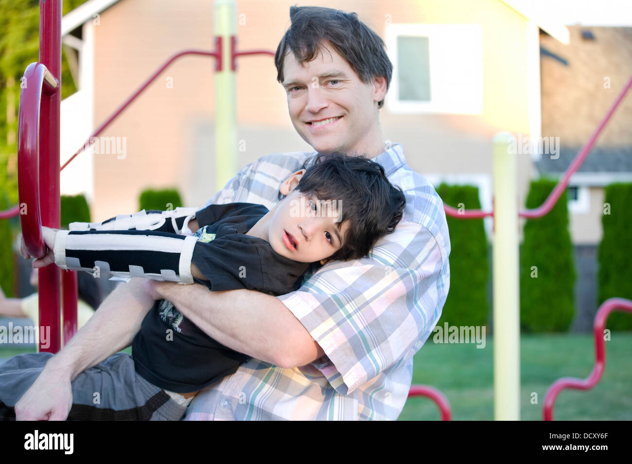 Father helping disabled son to play at playground Stock Photo - Alamy