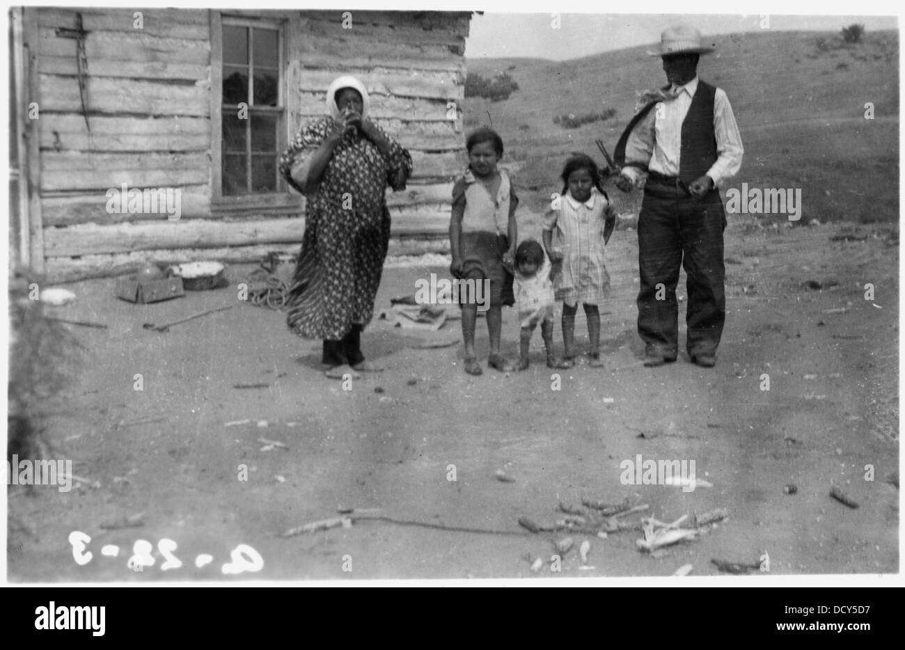 An Indian family stands in front of a log house, likely a traditional ...