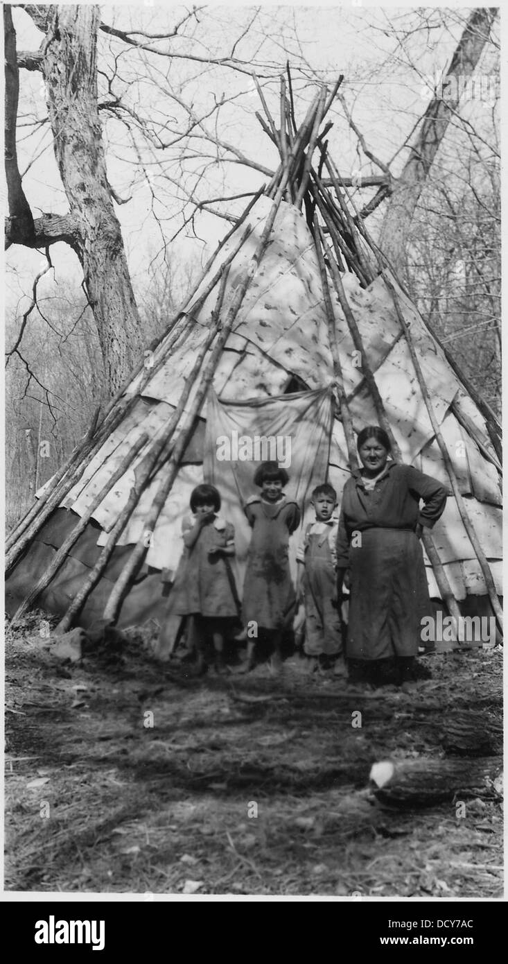 An Indian woman and her children stand in front of a teepee, a ...