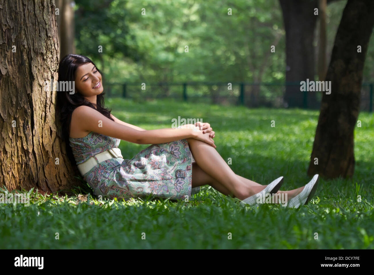 Young woman leaning against a tree Stock Photo - Alamy