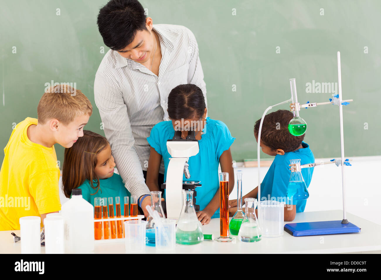 primary teacher and students in science class with young girl using ...