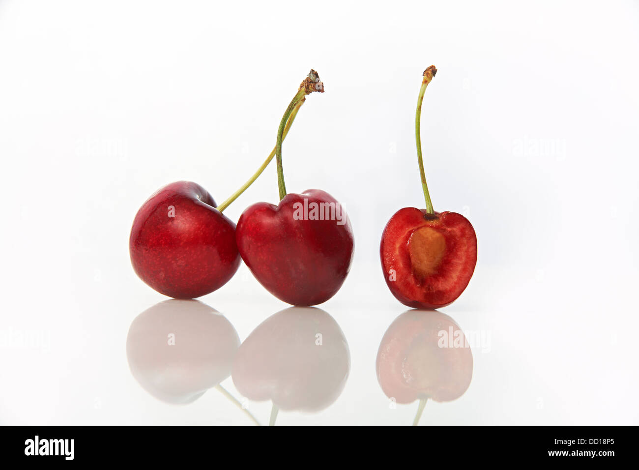 studio shot of red cherries on white background with one cut in halve ...