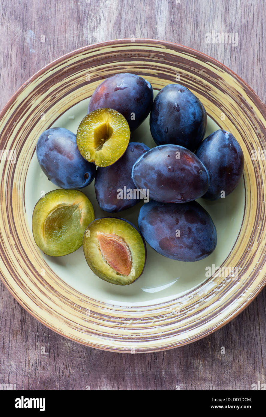 Fresh plums on plate over wooden background, overhead Stock Photo - Alamy
