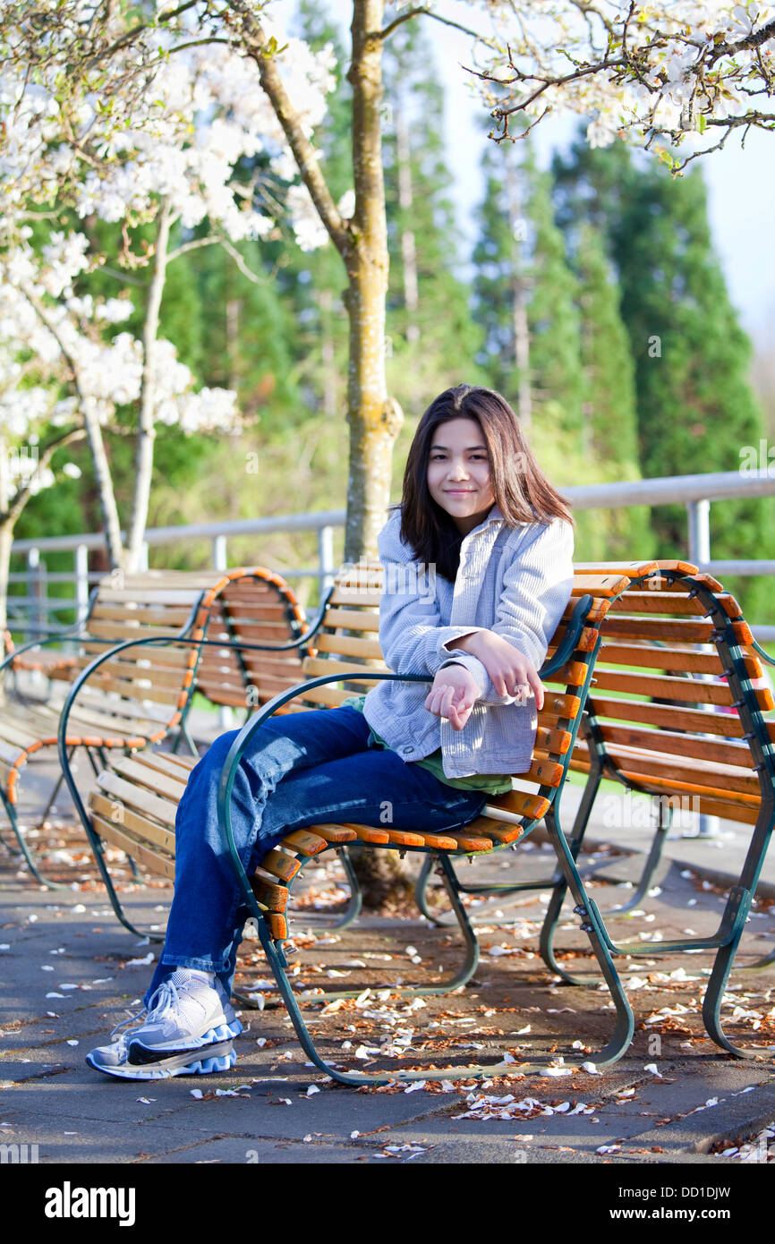 Young teen girl sitting on bench under cherry blossom tree Stock Photo ...