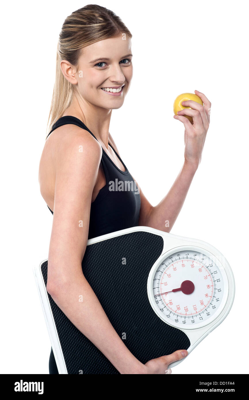 Young fitness girl holding fruit and weighing scale Stock Photo - Alamy