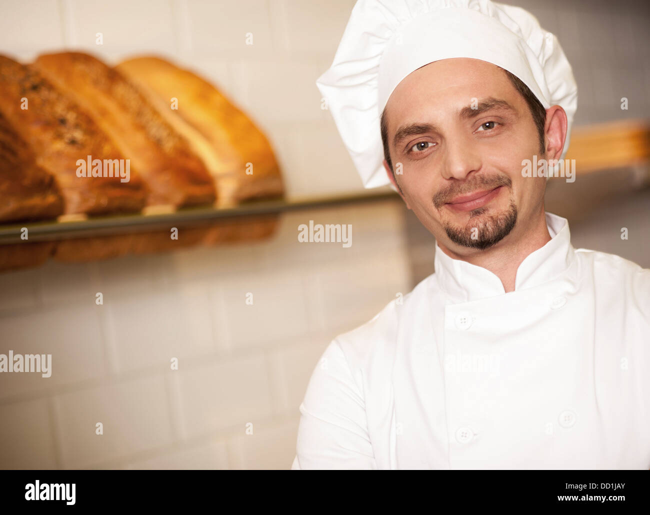 Smiling baker posing for the camera. Freshly baked breads in background ...