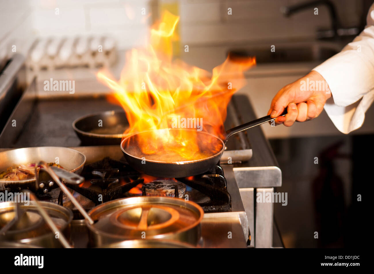 Chef cooking with flame in a frying pan on a kitchen stove Stock Photo ...