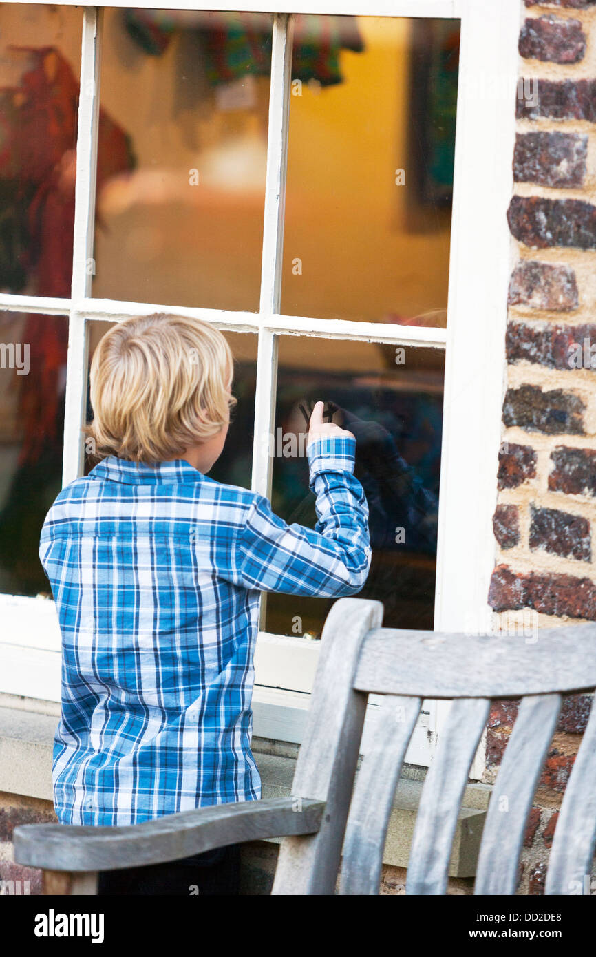Young boy drawing writing in mist from breath on window pane with ...