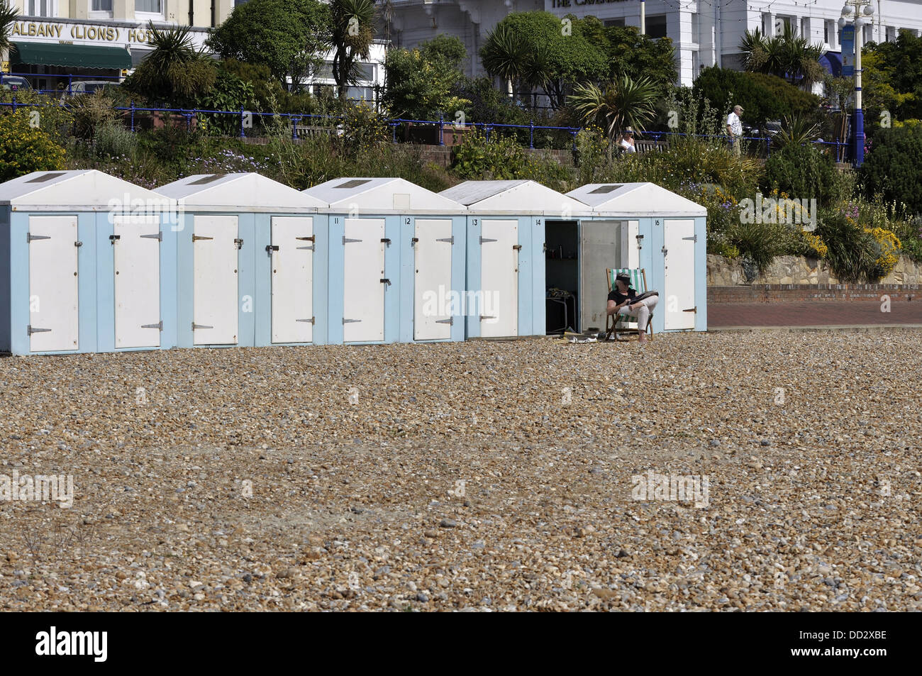 Private beach huts on Eastbourne beach with female sitting on deckchair ...