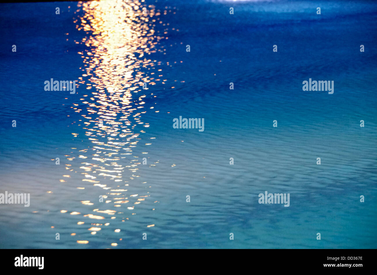 A beam of sunlight reflecting over rippled blue water with copyspace ...