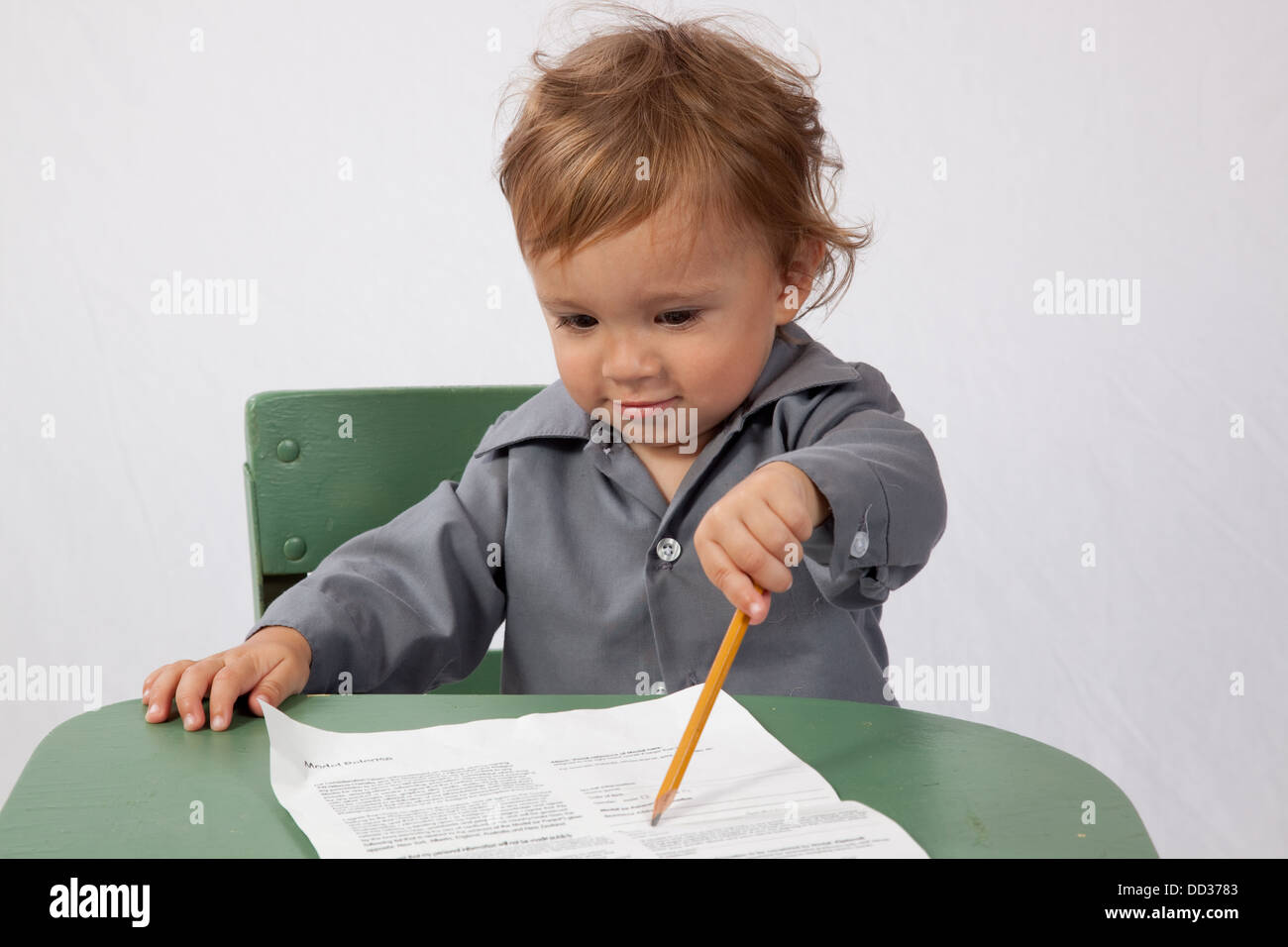 Young boy sitting at a desk with a sheet of paper and a pencil, looking ...