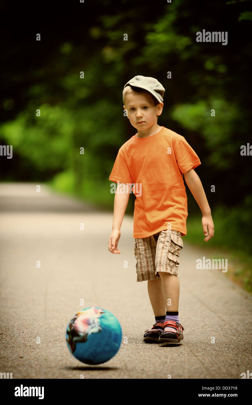 Boy young kid playing with ball kicks running towards ball in park ...