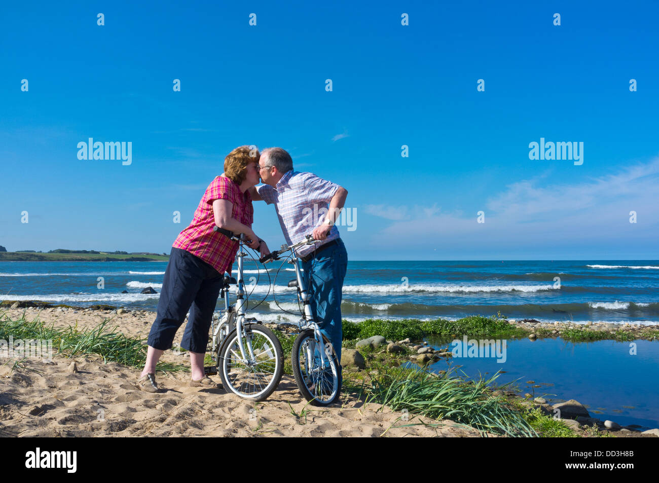 A Man And Woman Exchange A Kiss While On A Bike Ride Along The Water; Northumberland, England ...