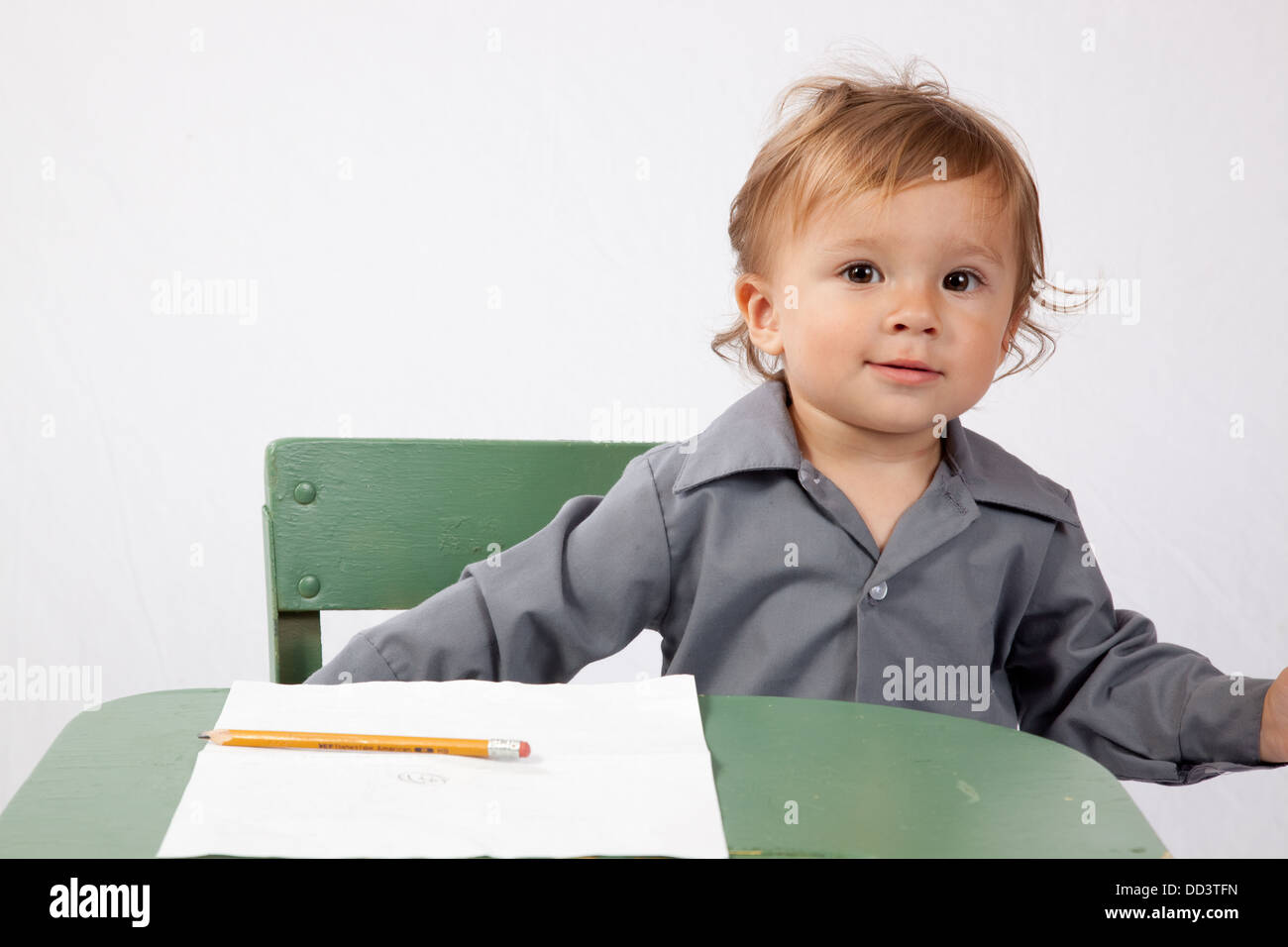 Young boy sitting at a desk with a piece of paper and a pencil, looking ...