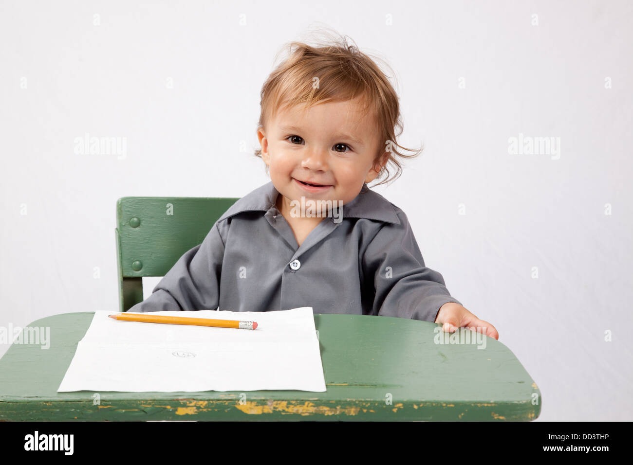 Young boy sitting at a desk with a piece of paper and a pencil, looking ...