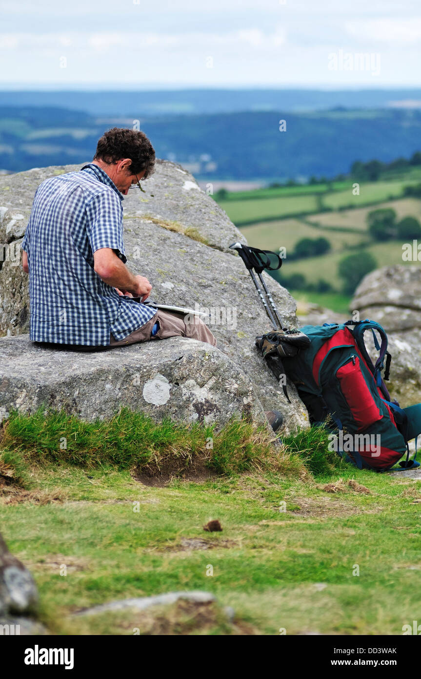 Walker sitting on a rock checking his map on Hound Tor in Dartmoor ...
