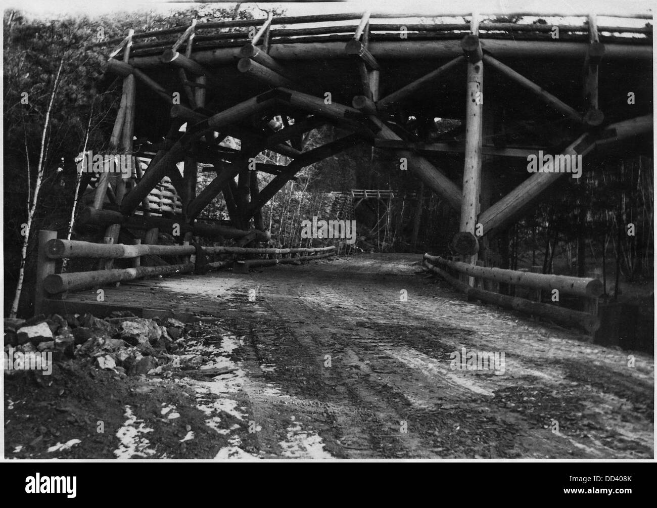This photograph captures a road passing under a log bridge, likely part ...