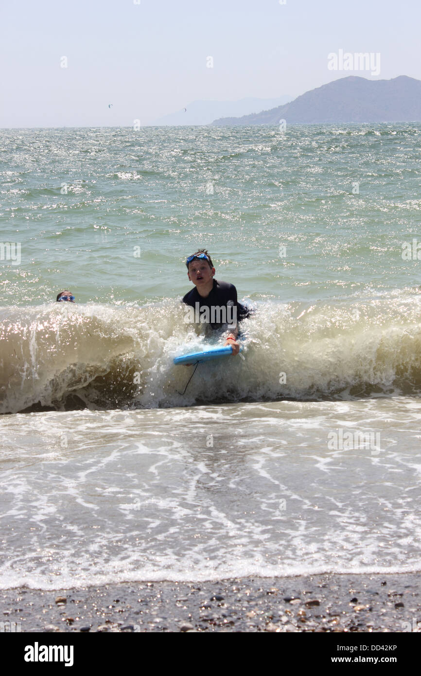 Two boys playing in the surf with a surfboard Stock Photo - Alamy