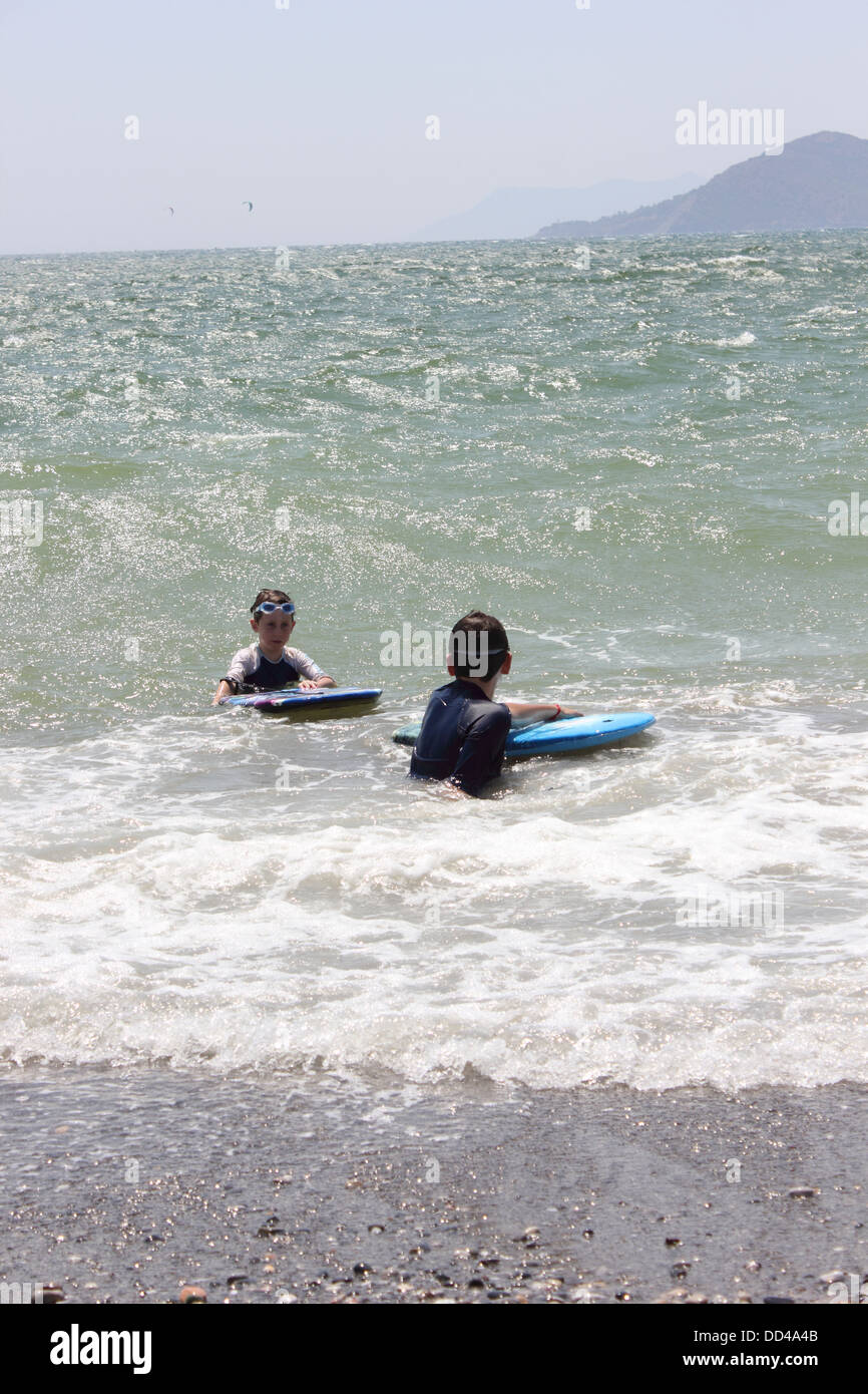 Two boys playing in the surf with a surfboard Stock Photo - Alamy