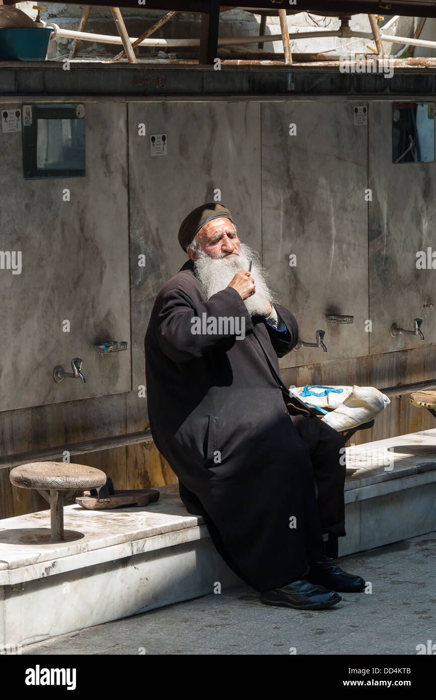A religious old man with traditional clothes combs his beard before ...