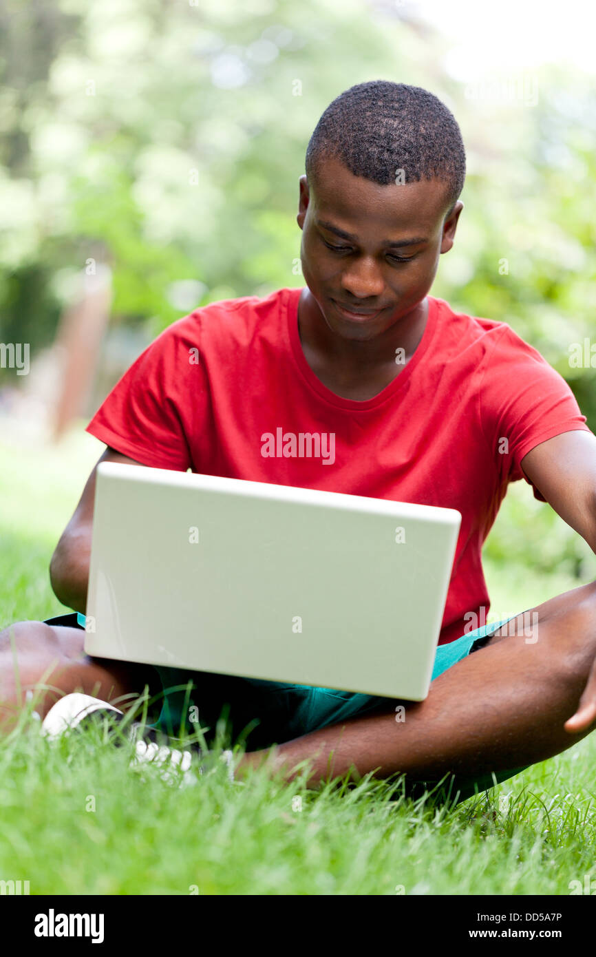 young smiling african student sitting in grass with notebook outdoor in ...