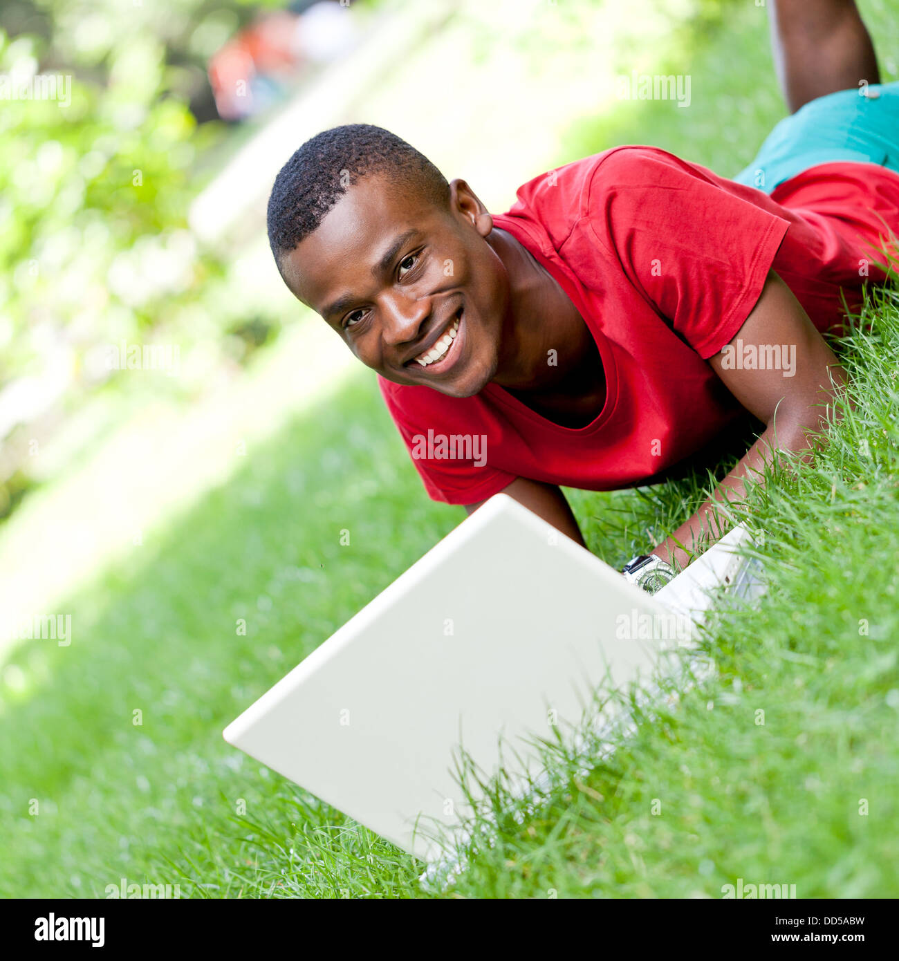 young smiling african student sitting in grass with notebook outdoor in ...