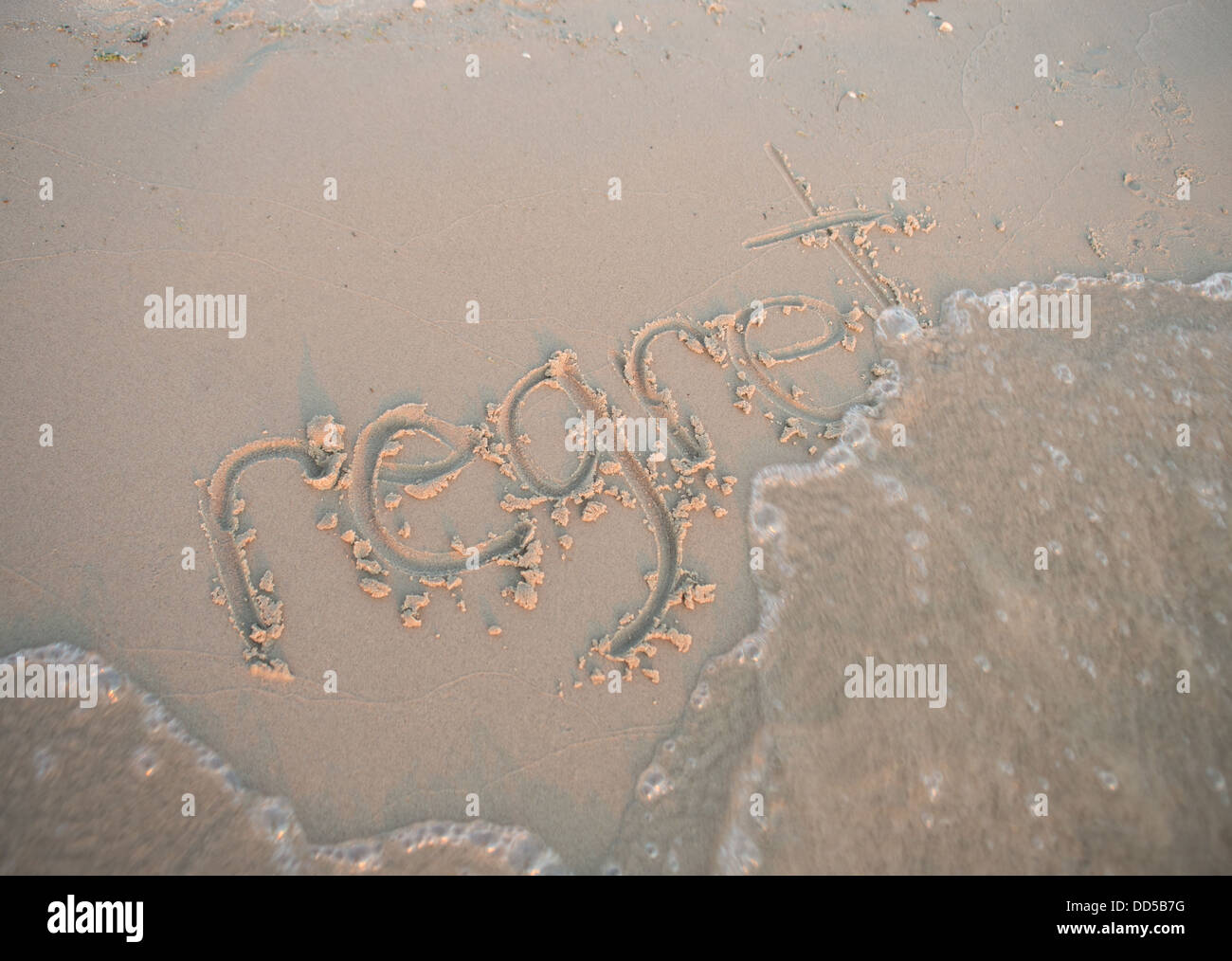 The word "regret" written in the sand, being washed away by a wave ...