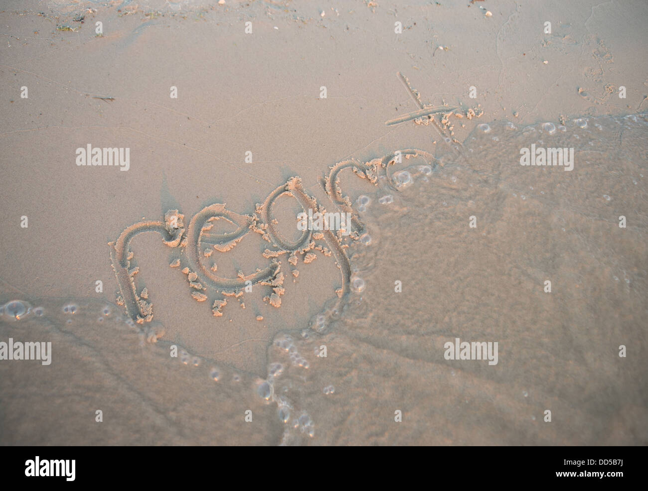 The word "regret" written in the sand, being washed away by a wave ...