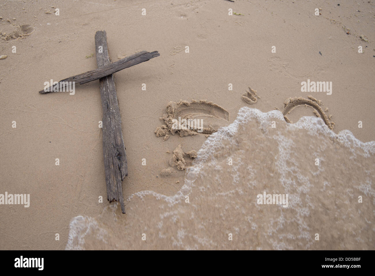 The word "sin" written in the sand next to a cross made of driftwood ...