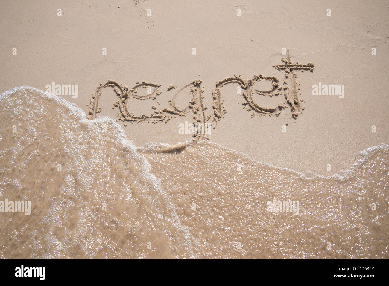 The word "regret" written in the sand, being washed away by a wave ...