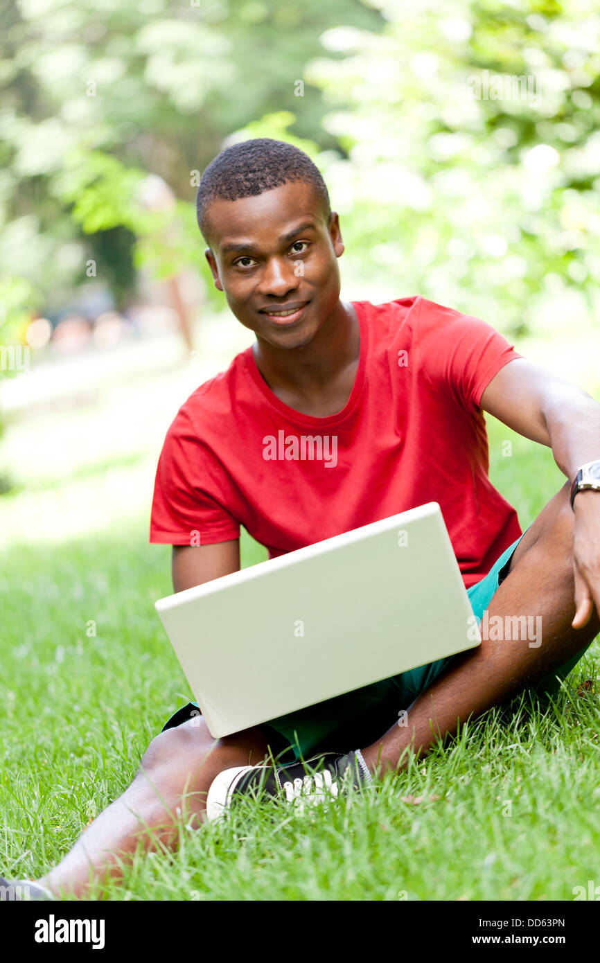 young smiling african student sitting in grass with notebook outdoor in ...