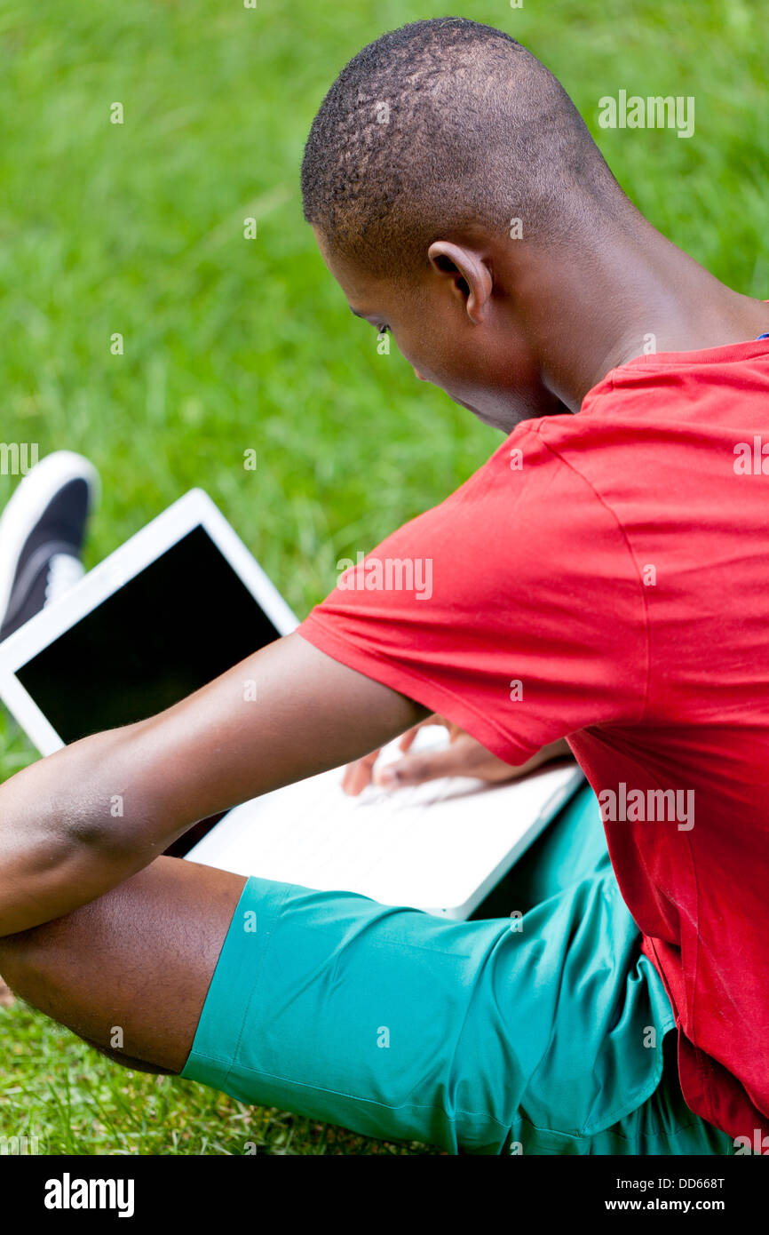 young smiling african student sitting in grass with notebook outdoor in ...