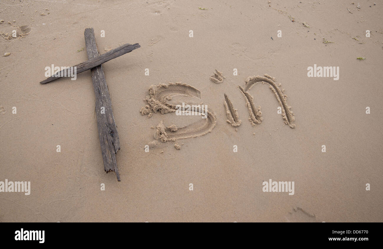 The word "sin" written in the sand next to a cross made of driftwood ...