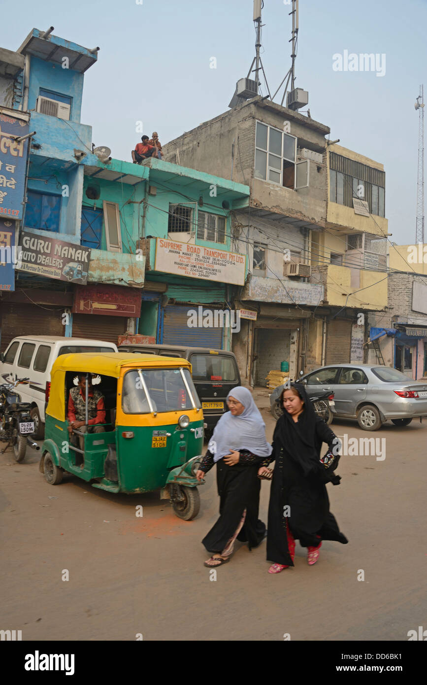 Two Muslim girls walk past a Tut-tut in a slum district of Old Delhi in ...