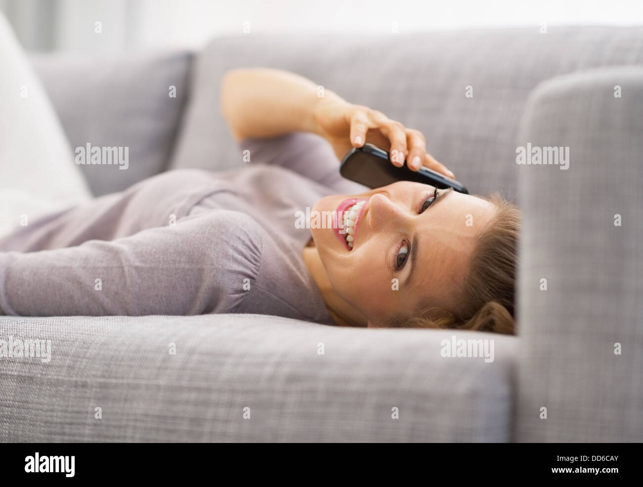 Smiling young woman talking mobile phone while laying on couch Stock ...